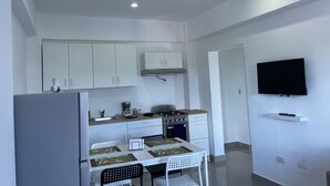 Cozinha compacta com armários brancos, fogão a gás, geladeira e área de jantar com duas cadeiras e uma mesa.