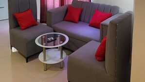 Uma sala de estar moderna com um sofá cinza, almofadas vermelhas e uma mesa de centro de vidro.