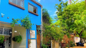 Um edifício azul com entrada de vidro, uma placa e um caminho de terra.