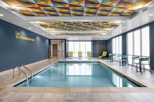 Piscina interna com design geométrico no teto, área de estar com cadeiras e espaço à beira da piscina.