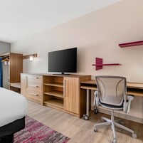 Quarto moderno com cama, escrivaninha, computador, televisão e cadeira.