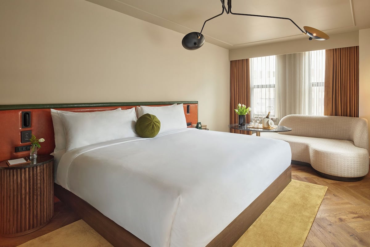 Quarto de hotel com uma cama grande, um sofá, uma escrivaninha com abajur e vista para o exterior pela janela.