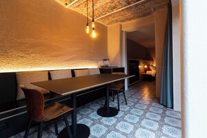Uma área de jantar moderna com uma mesa comprida, assentos acolchoados e luminárias pendentes.