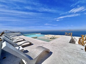 Uma piscina infinita no terraço, com espreguiçadeiras e vista para o oceano.