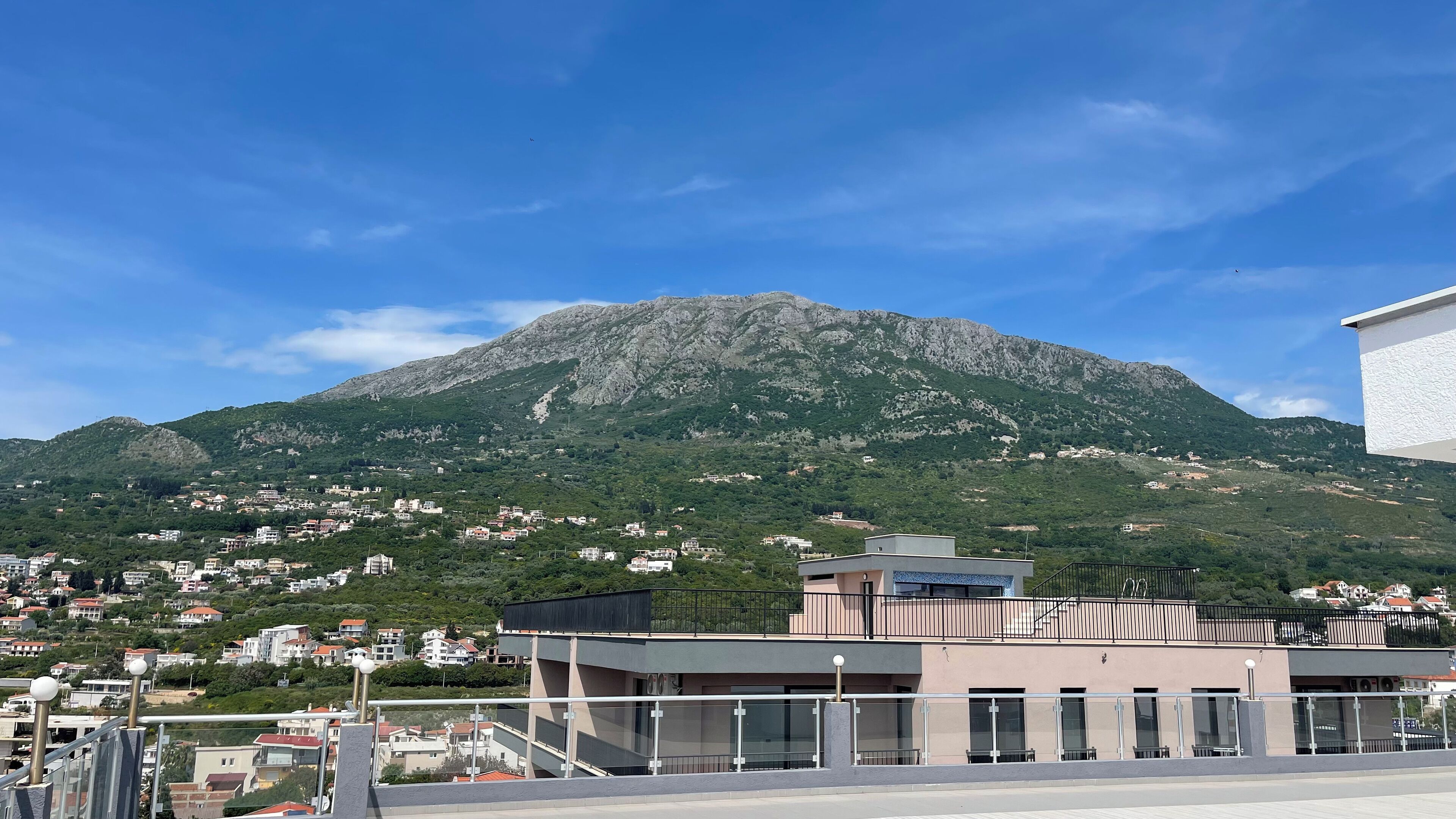 Um edifício moderno com telhado plano e varanda, com vista para uma paisagem montanhosa e casas dispersas.