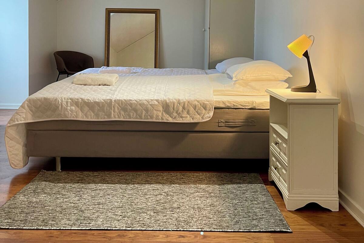 Quarto com cama, mesa de cabeceira, espelho e claraboia.