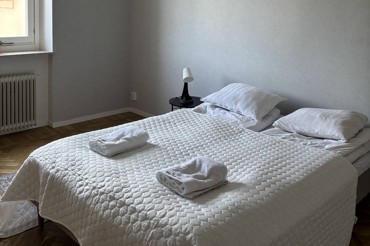 Quarto com cama, mesa de cabeceira, abajur e janela.