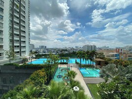 Área de piscina no terraço com várias piscinas, cercada por palmeiras e vegetação, com vista para um horizonte urbano de arranha-céus.
