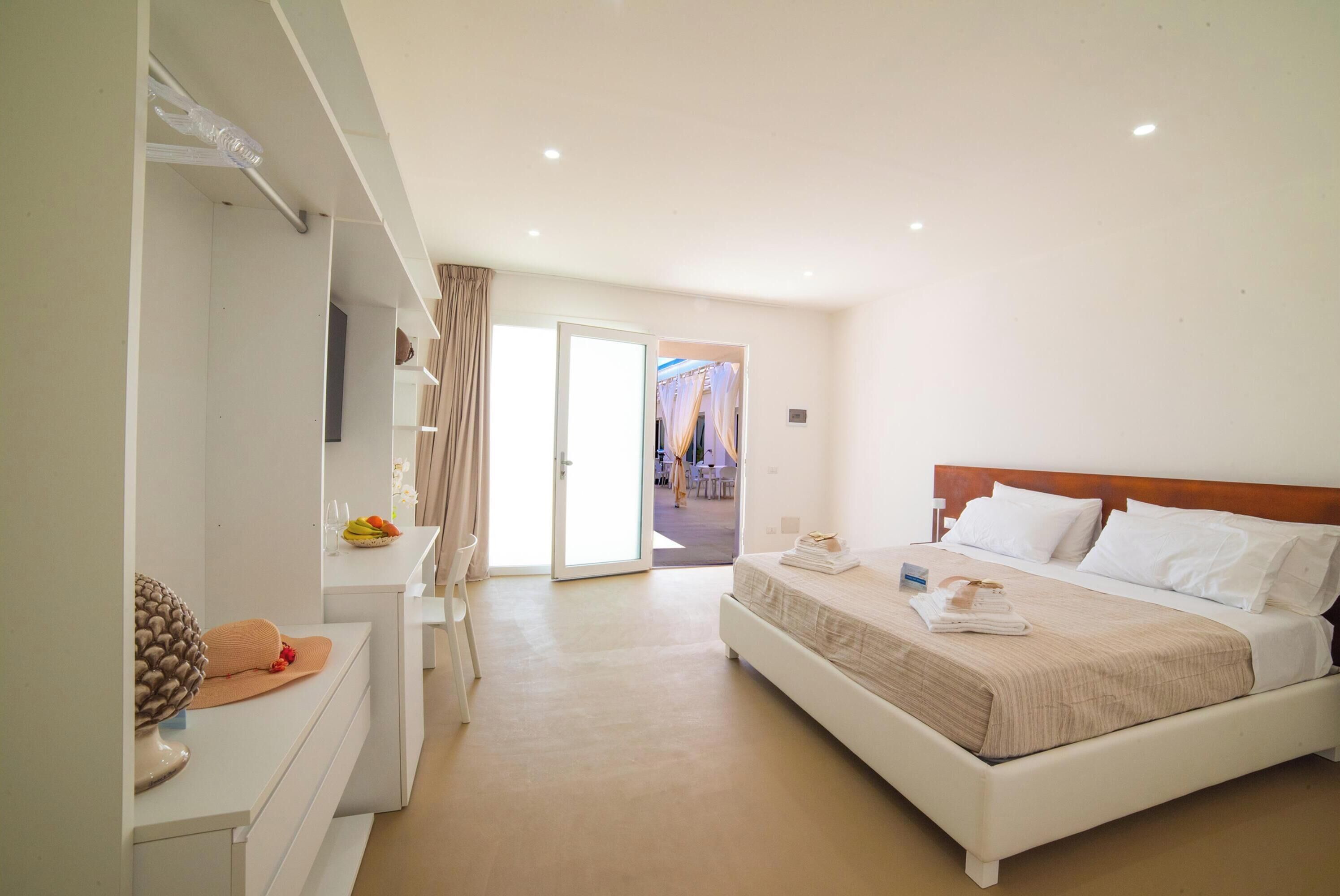 Quarto de hotel com cama, escrivaninha, cadeira, armário e porta que dá para um corredor.