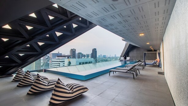 Área de piscina no terraço com almofadas listradas, barreira de vidro e vista para o horizonte da cidade.