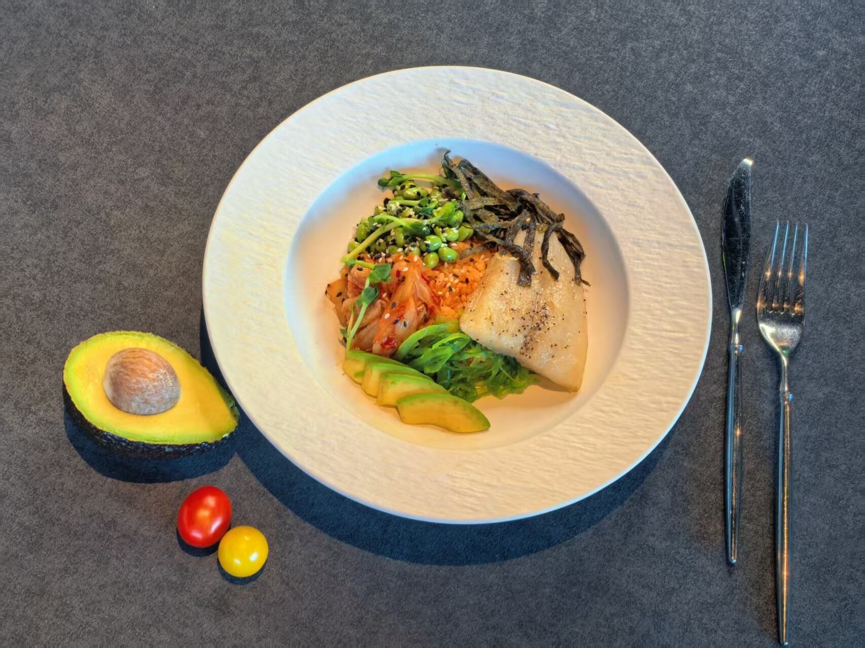 Um prato com filé de peixe, abacate e folhas verdes sobre uma superfície escura.