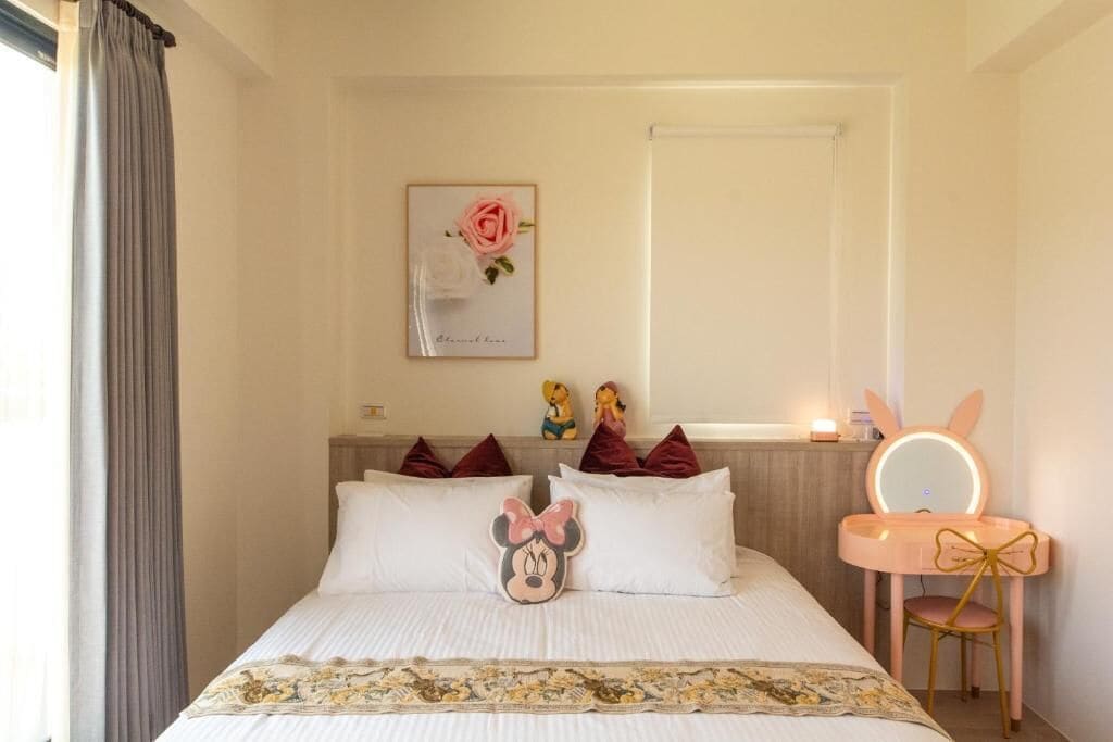 Quarto de hotel com uma cama, uma mesa de toucador com espelho e uma imagem emoldurada de uma rosa na parede.