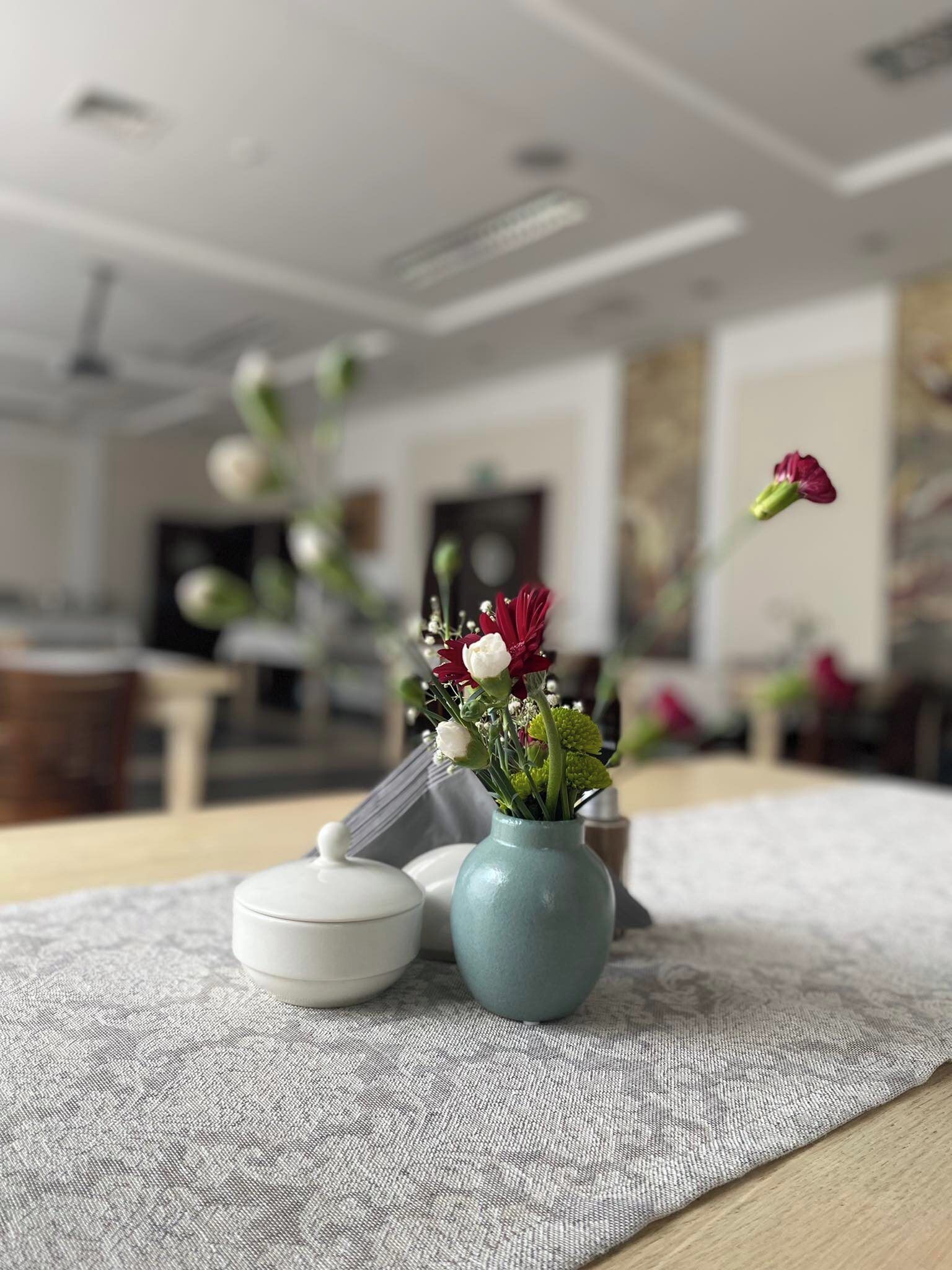 Uma mesa de jantar com um vaso de flores, um recipiente branco e um recipiente azul.
