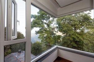 Quarto com uma janela grande, vista para árvores e um canto com piso de madeira.