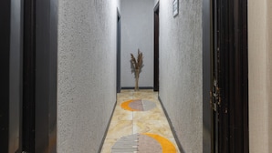 Um corredor com paredes texturizadas, piso estampado e um vão de porta à direita.