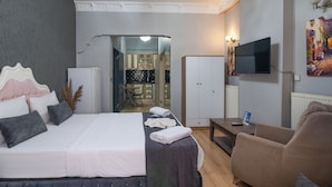 Quarto com cama, televisão, sofá e uma pequena cozinha ao fundo.