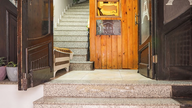 Entrada de hotel com porta de madeira, escadaria que leva ao interior e placa indicando 'Nest Suite'.