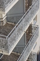 Varanda externa com vários níveis, grade de metal detalhada e piso de madeira.