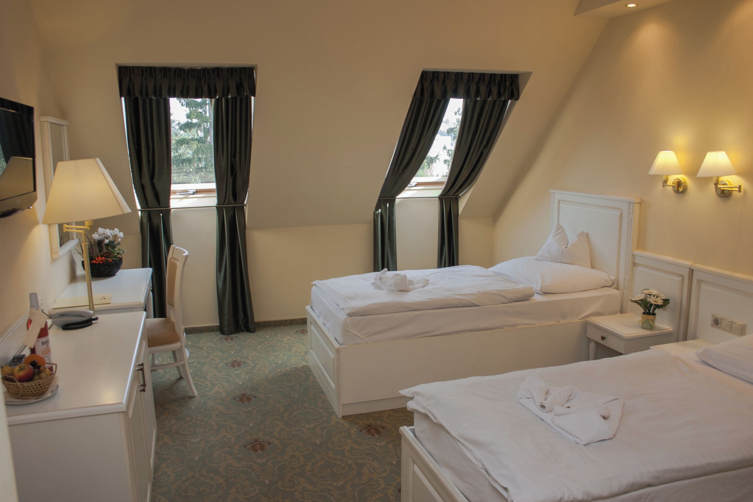 Quarto de hotel com duas camas, uma escrivaninha com abajur e uma cadeira.