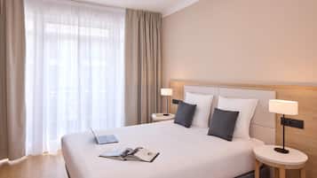 Quarto de hotel com uma cama grande, duas mesas de cabeceira, um laptop e um livro sobre a cama.