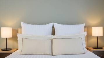 Uma cama bem arrumada com lençóis brancos e duas luminárias de cabeceira em mesas de cabeceira de madeira.