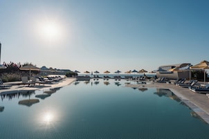 Área de piscina com espreguiçadeiras e guarda-sóis, sob um céu claro.