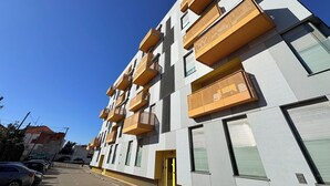 Um edifício moderno de vários andares com varandas, céu limpo e carros estacionados.