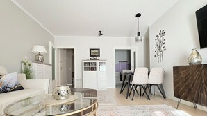 Uma sala de estar moderna com uma mesa de centro de vidro, sofá branco e um espaço de jantar com cadeiras.