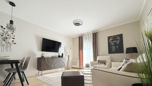 Uma sala de estar moderna com um sofá, televisão, área de jantar com cadeiras e mesa, e um objeto decorativo na parede.