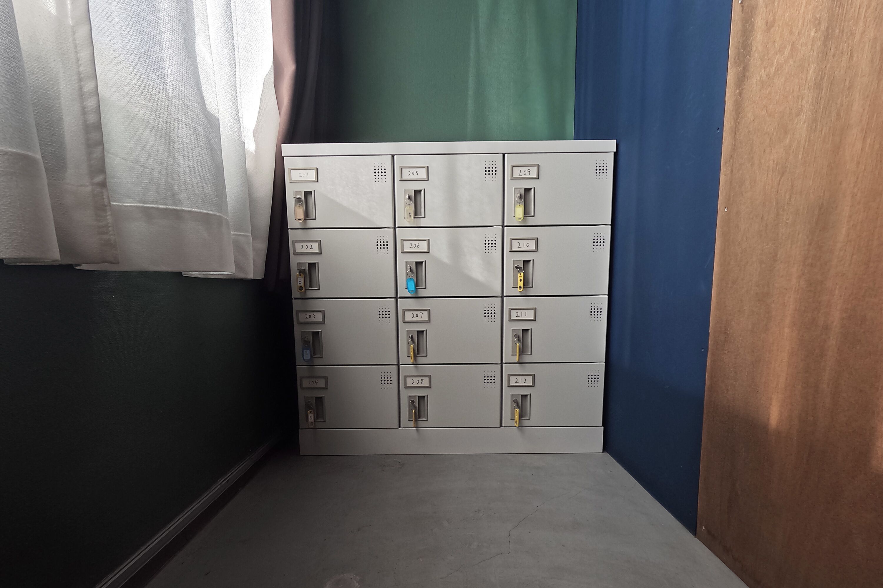 Uma fileira de armários de metal com compartimentos numerados, uma parede azul e uma porta de madeira.