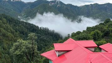 Paisagem montanhosa com um edifício de telhado vermelho, rodeado por vegetação exuberante.