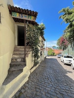 Uma rua de paralelepípedos leva a um edifício com uma placa que diz 'CORES DA PIPA'.
