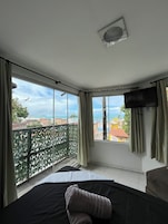 Quarto com cama, televisão e varanda com vista para edifícios e o mar.
