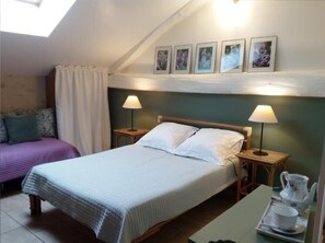 Quarto com cama, duas mesas de cabeceira, um criado-mudo, janela com cortinas e um quadro na parede.