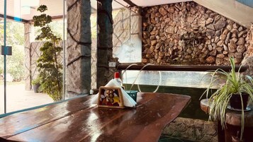 Mesa de madeira com uma garrafa de plástico e um objeto decorativo, uma planta em vaso e uma parede de pedra com um recurso de água.