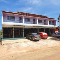 Edifício de dois andares com telhado plano e antena parabólica. Dois carros estão estacionados em frente.