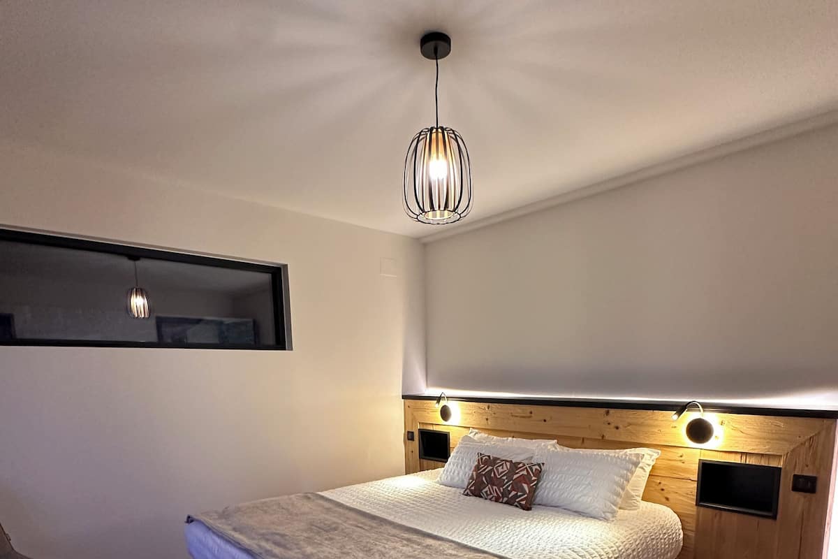 Quarto moderno com uma cama grande, cabeceira de madeira, televisão integrada e uma luminária pendente singular.