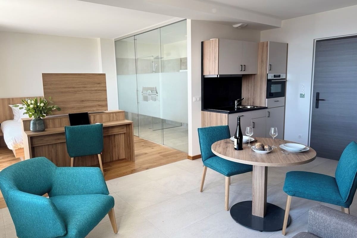Quarto de hotel moderno com área de jantar, cozinha e porta de vidro deslizante para uma varanda.