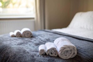 Cama arrumada com toalhas brancas dobradas e um cobertor cinzento.