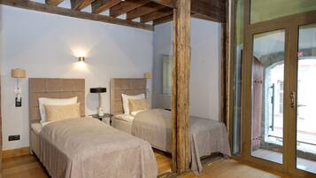 Quarto com duas camas, vigas de madeira no teto, luminária fixada na parede e porta de vidro deslizante para o exterior.