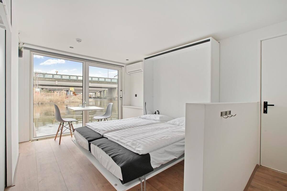 Quarto moderno com uma cama grande, uma mesinha e uma cadeira perto de uma porta de correr de vidro.