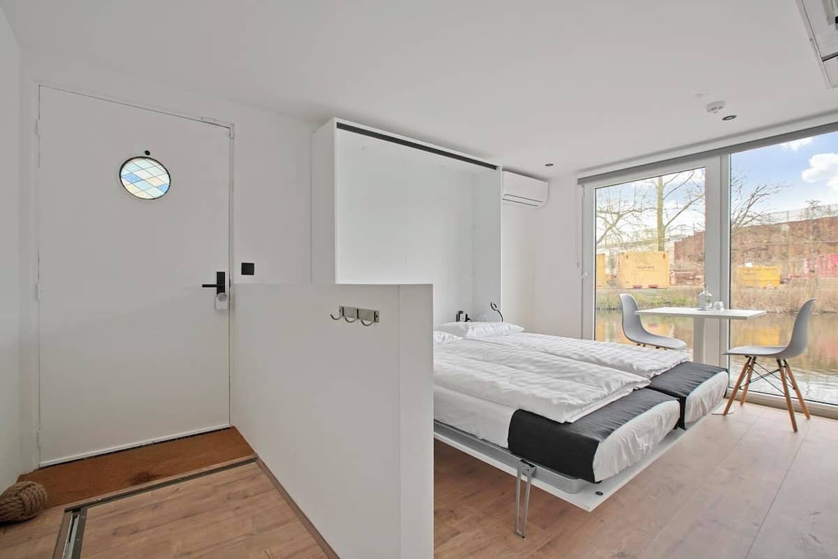 Quarto moderno com cama, uma mesa pequena e uma cadeira perto de uma janela com vista para um rio.
