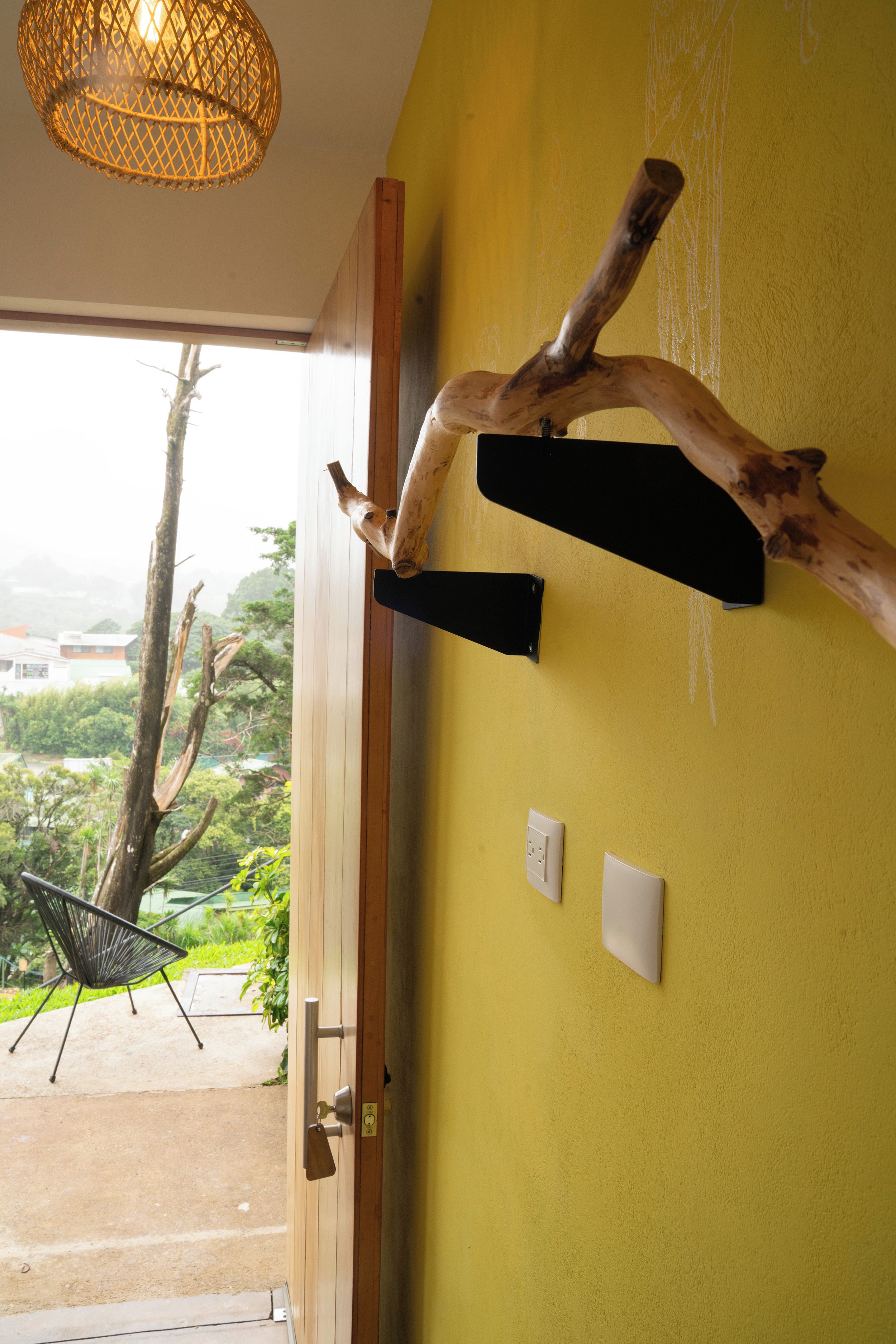 Um quarto com parede amarela, porta de madeira, banco de metal preto e luminária pendente.