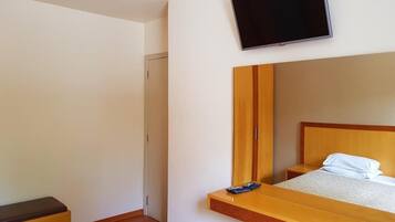 Quarto com cama, televisão fixada na parede e um banco.