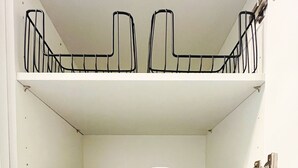 Uma cozinha com forno embutido e micro-ondas, bancada branca e prateleira superior em metal.