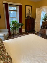 Quarto com uma cama grande, penteadeira, cadeira, janela com cortinas vermelhas e planta em vaso.
