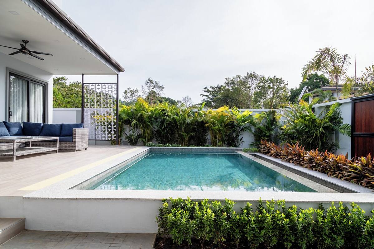 Uma área de piscina moderna ao ar livre, com espaço de estar integrado, cercada por vegetação exuberante e uma piscina azul cristalina.