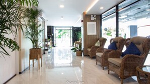 Um lobby moderno com sofás de vime, plantas em vasos e um painel de vidro com vista para o exterior.