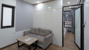 Quarto moderno com sofá cinzento, uma pequena mesa de madeira e porta de vidro para uma varanda.