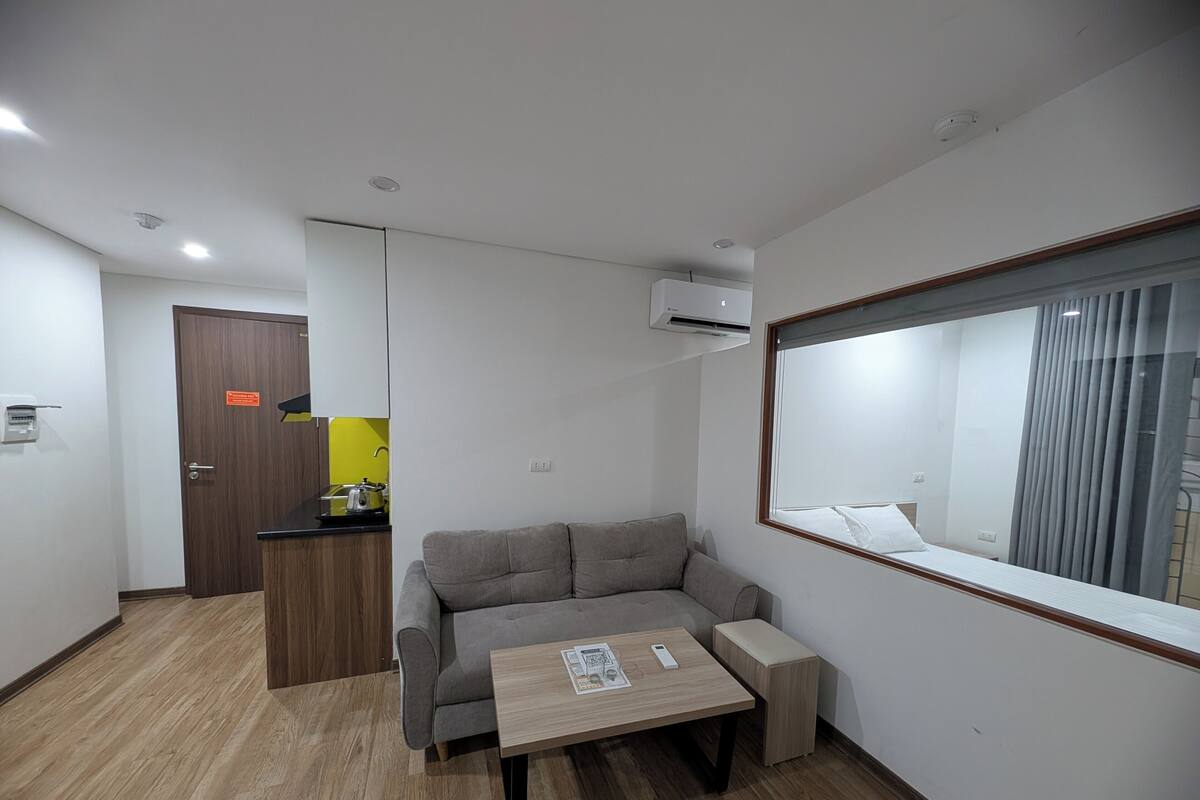 Um espaço de estar compacto com sofá, uma mesa pequena, cozinha compacta e uma janela grande.